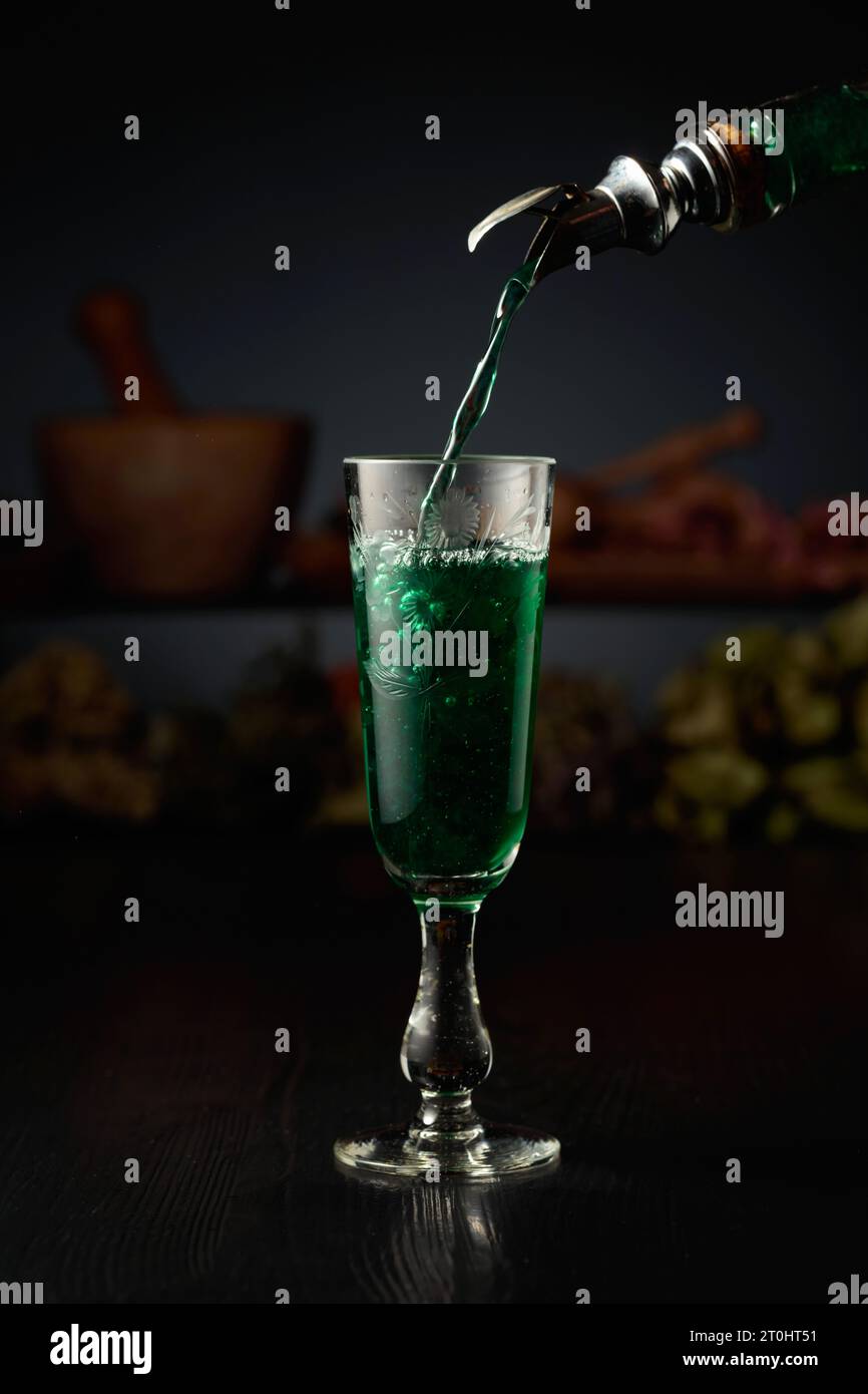 Green herbal liquor is poured from a vintage bottle into a glass. In ...