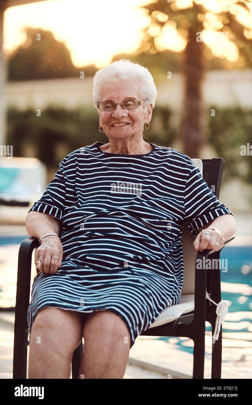 Unfiltered portrait, a real elderly woman sits gracefully in a chair ...