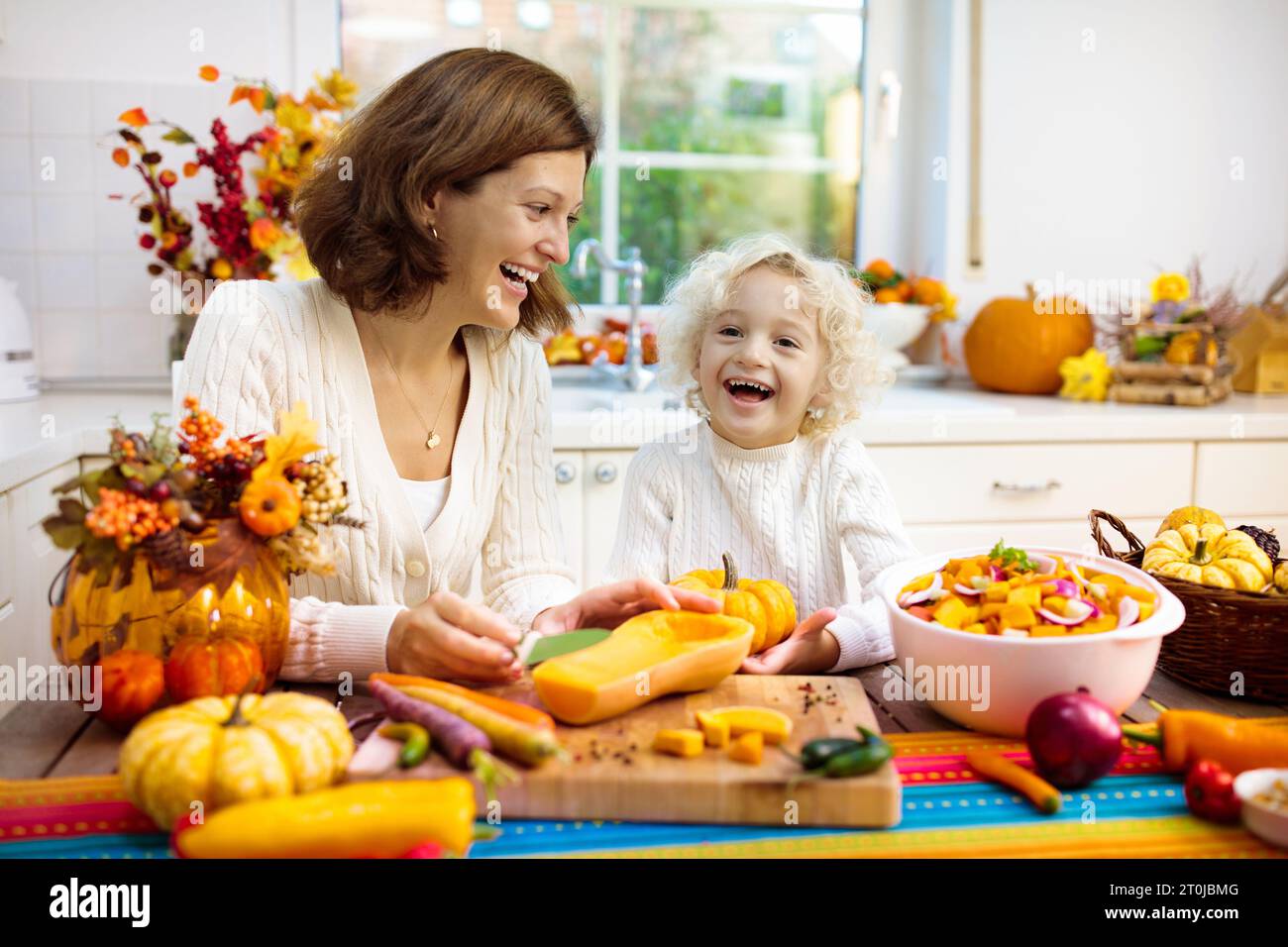Mother and son cutting pumpkin, onion and carrot, cooking soup for ...