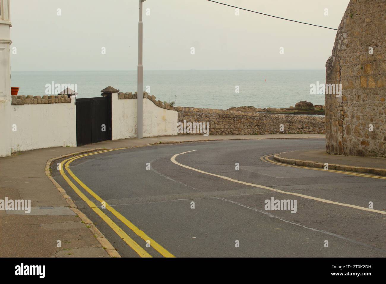 A photo of a road corner bending around a wall with a sea landscape in ...