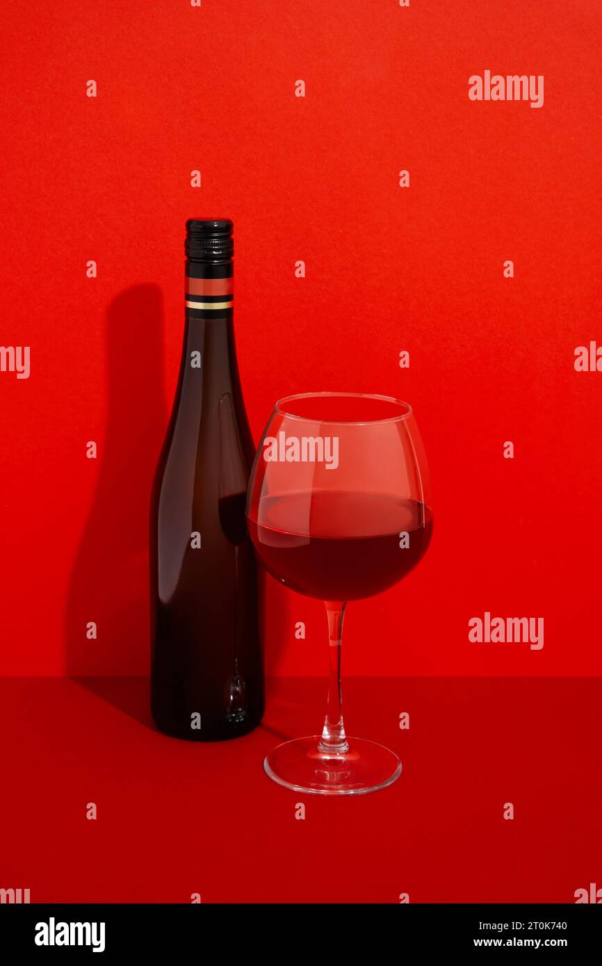 Bottle and glass of wine. Alcoholic drink on red background with deep ...