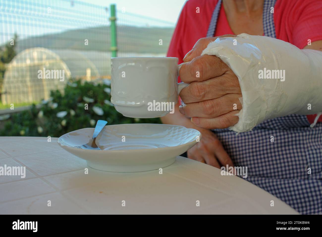 old woman with a cast in her wrist having a cup of coffee in her garden ...