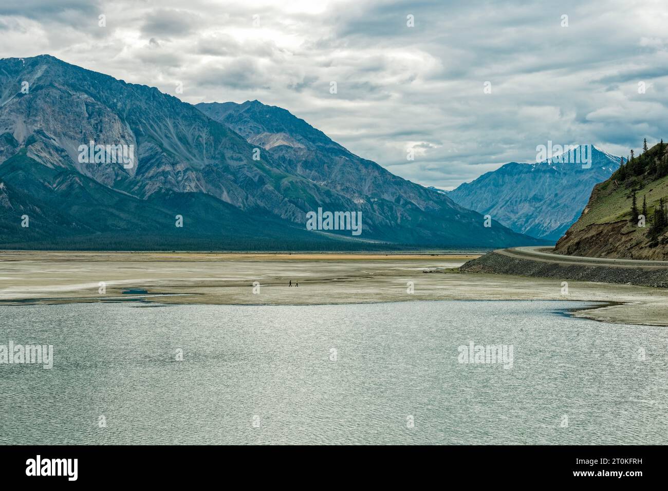 Distant hikers walk along the dry portion of the lakebed of Kluane Lake ...