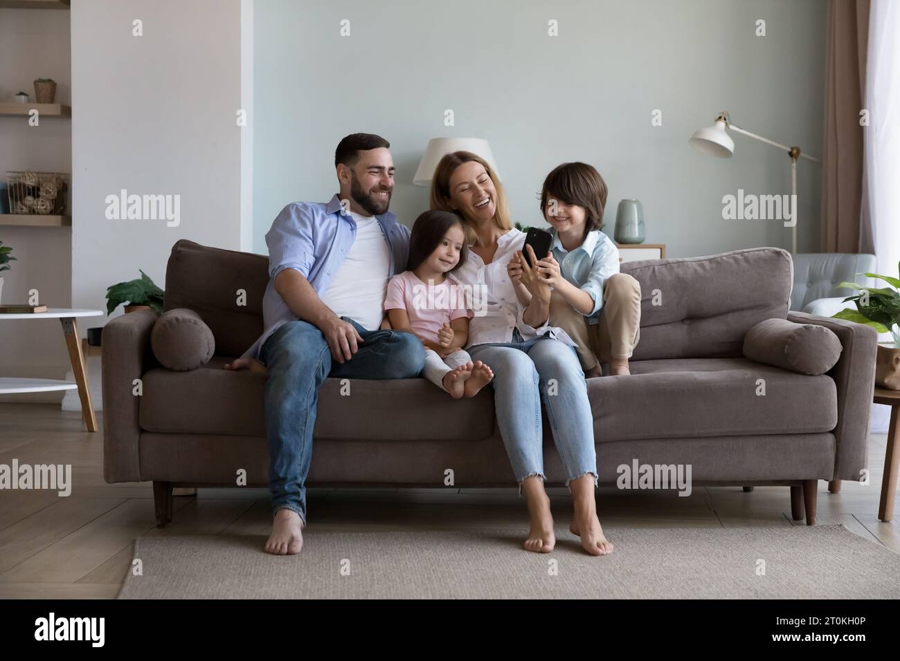 Happy millennial parents and two little children using mobile phone ...