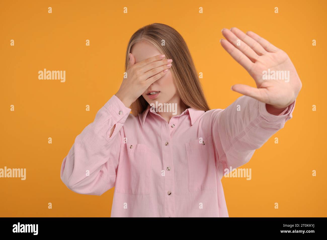 Embarrassed woman covering face with hand on orange background Stock ...