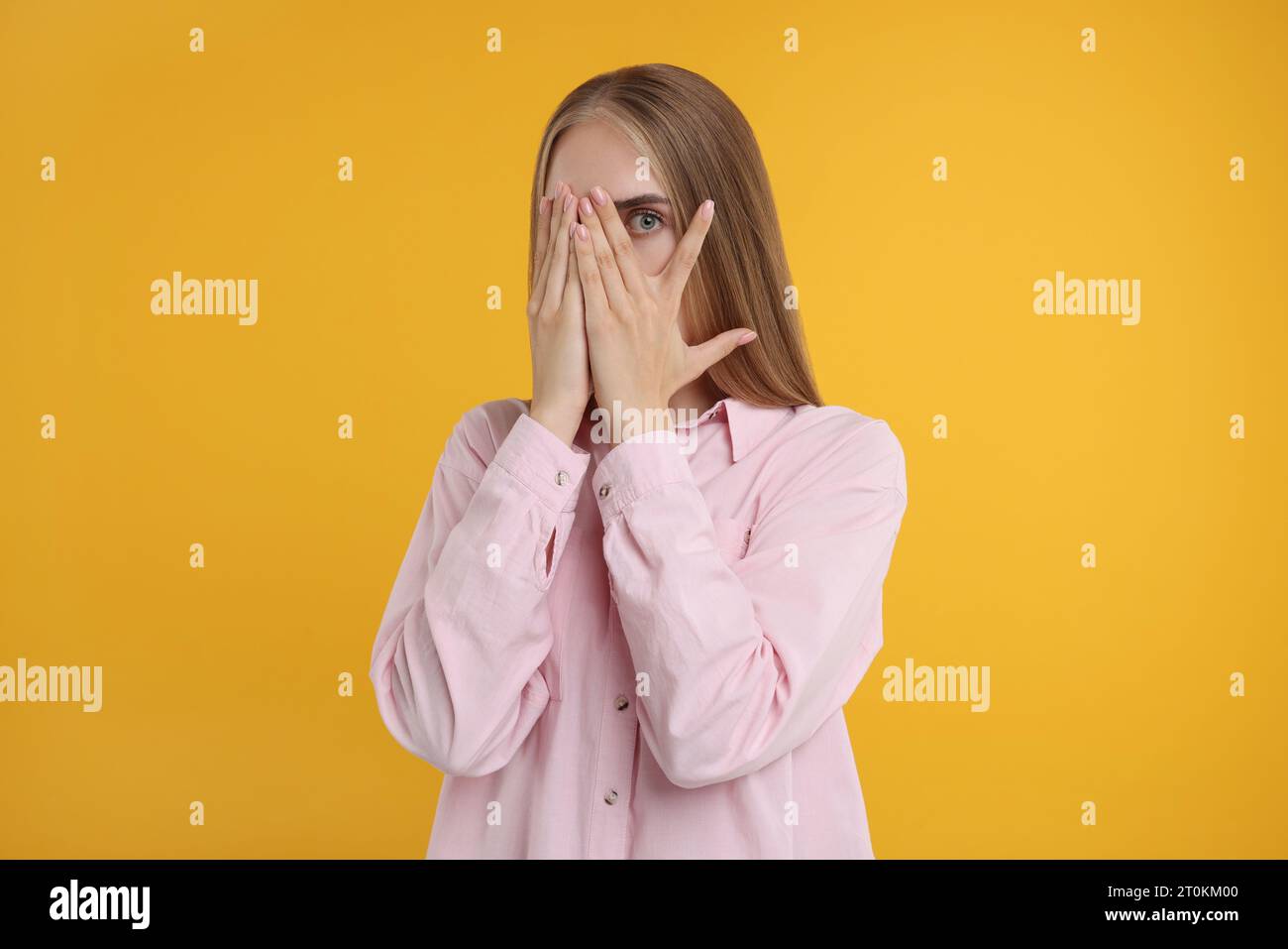 Embarrassed woman covering face with hands on orange background Stock ...