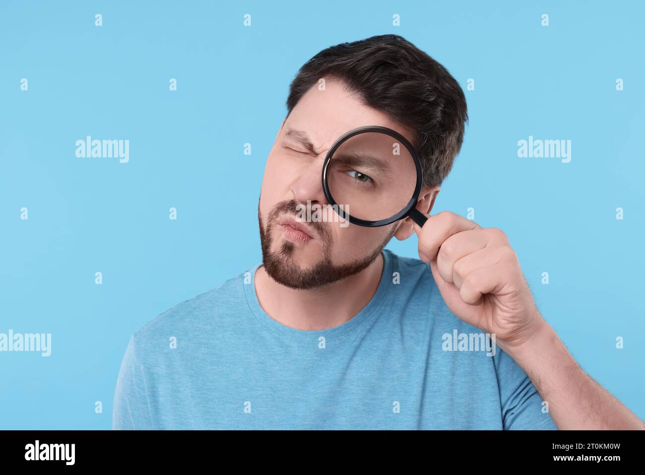 Confused man looking through magnifier glass on light blue background ...