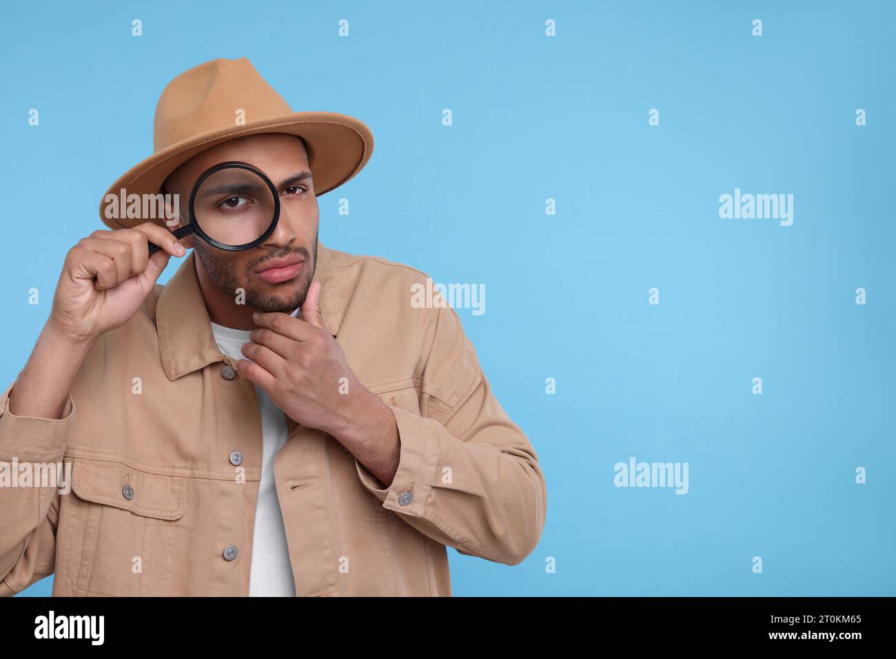 Curious man looking through magnifier glass on light blue background ...