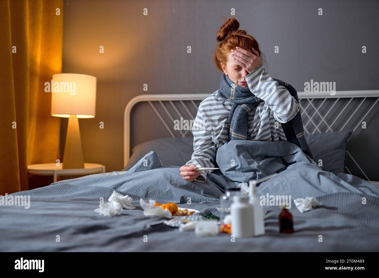 Young sick woman is holding the thermometer, touching her forehead ...