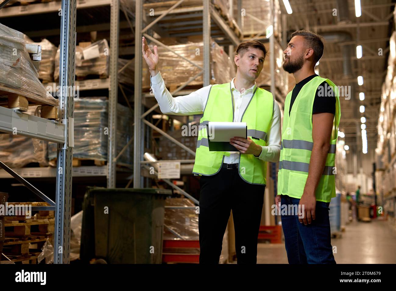 Caucasian two engineers in uniform, checking goods and supplies on shelves in warehouse ...