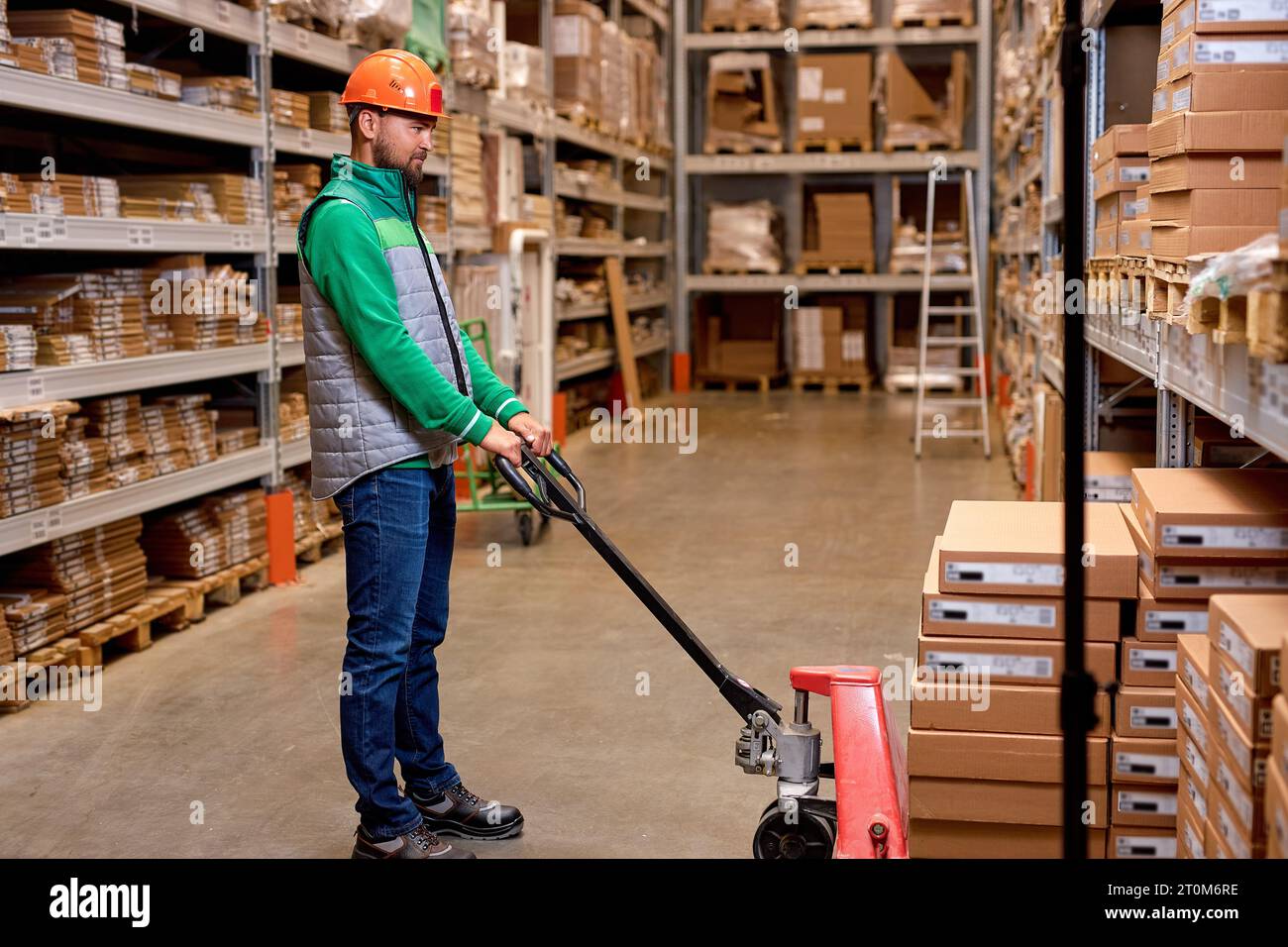 male staff worker in warehouse uses hand pallet stacker to transport ...