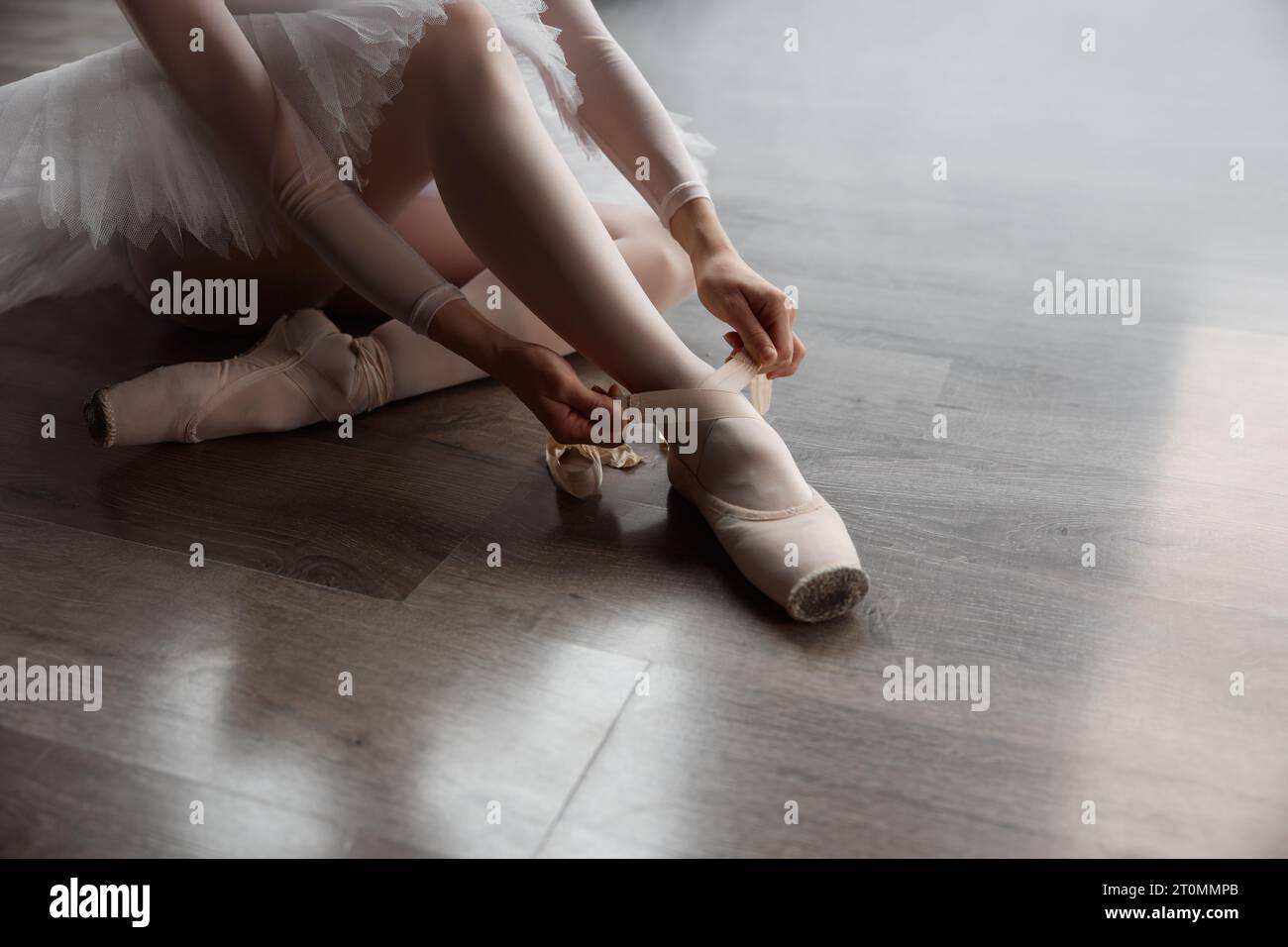 Ballerina sitting on floor putting on pointe shoes before choreography ...