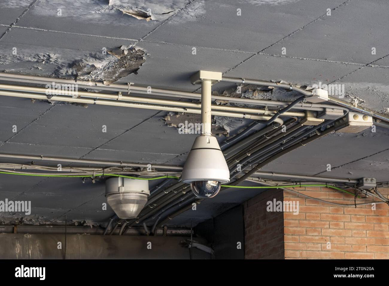 Surveillance camera hanging from the ceiling in an area with peeling ...