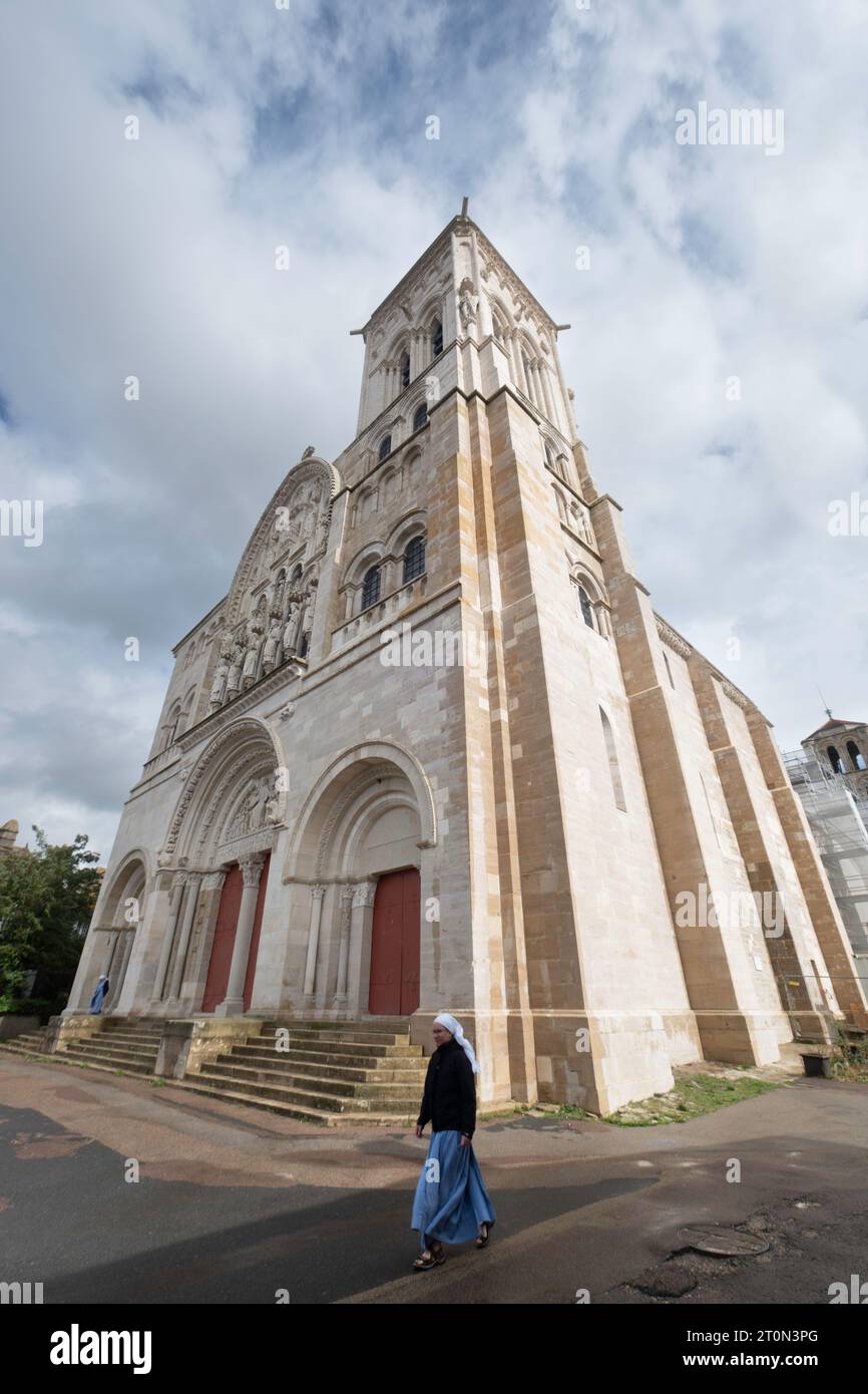 A nun walks past the facade of the Benedictine and Cluniac abbey church ...