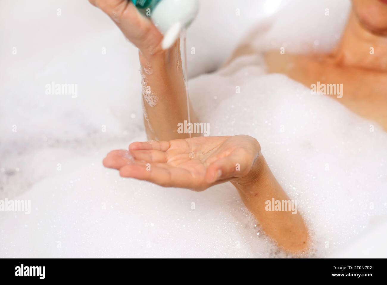 A woman takes a bath with foam. She pours gel onto her palm in the ...