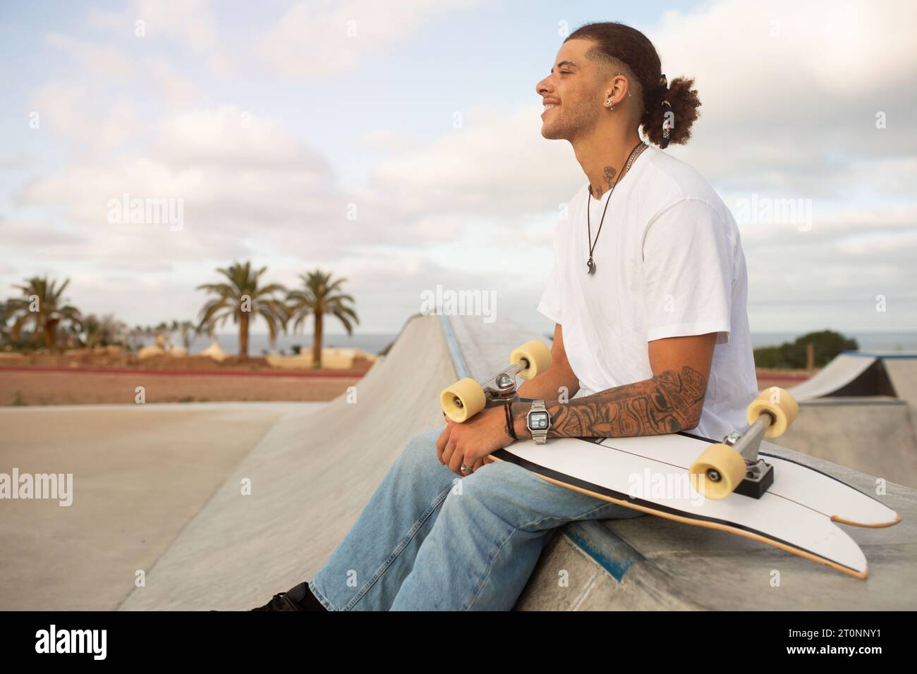 Skateboarder man resting, seating with board on ramp Stock Photo - Alamy