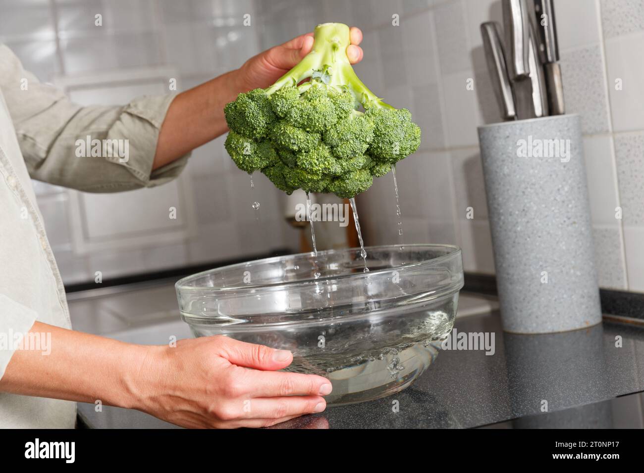 Female hands washing broccoli in a transparent glass bowl. Healthy food ...
