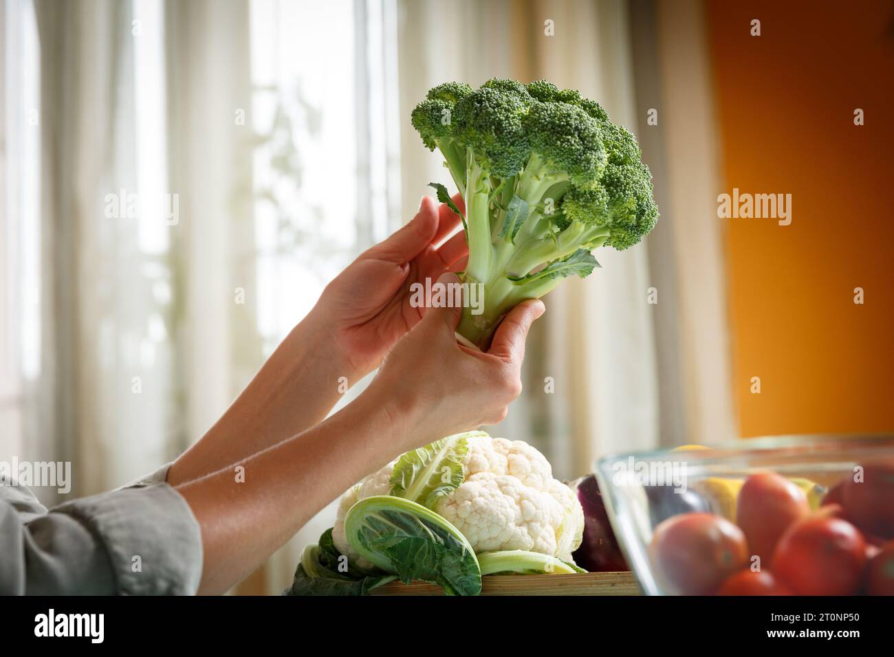 Female hands holding broccoli on a kitchen background together with ...