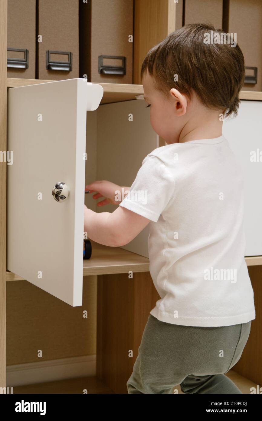 Toddler baby opens the closet door in the home living room. A small ...