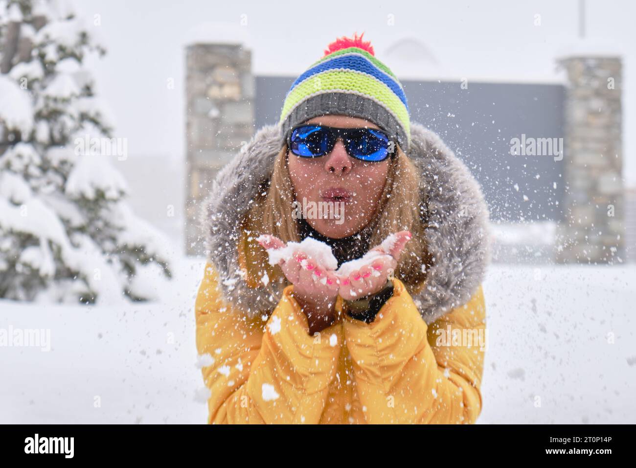 Woman blowing snow from her hands, wearing colorful yellow clothes in ...