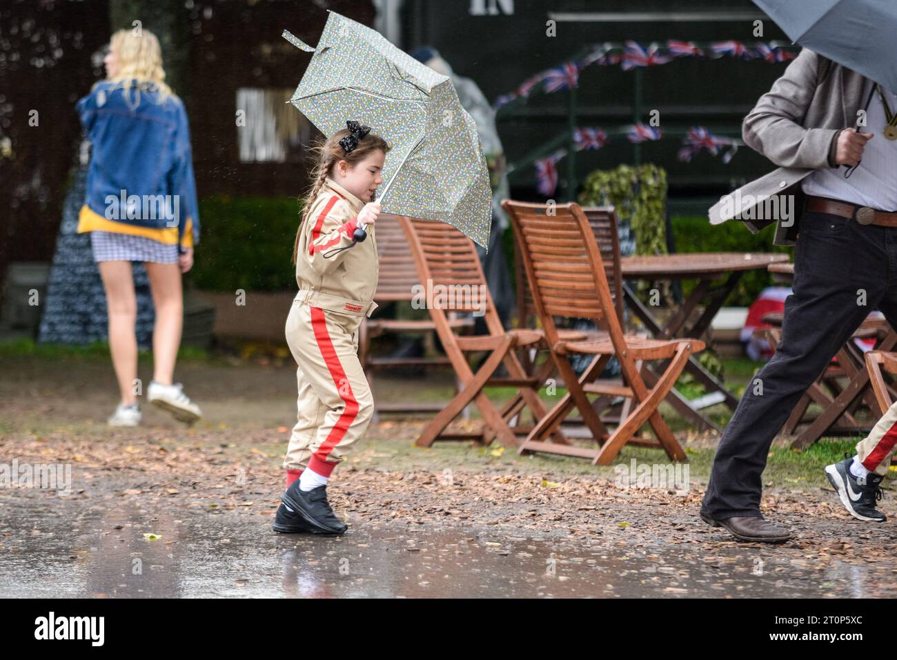Young girl in vintage racing overalls struggling against the weather ...
