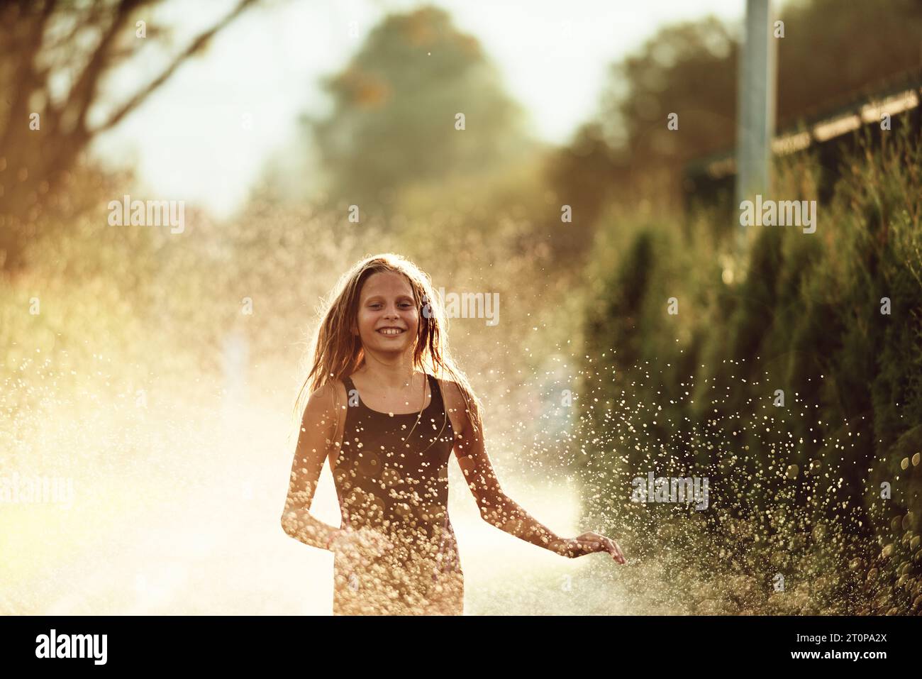 In the backyard of house, a young girl bursts with laughter and joy as she gleefully runs ...