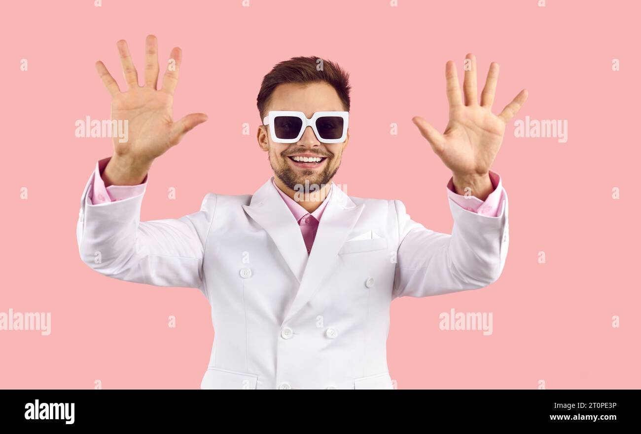 Happy handsome actor in white suit and sunglasses waving both his hands ...