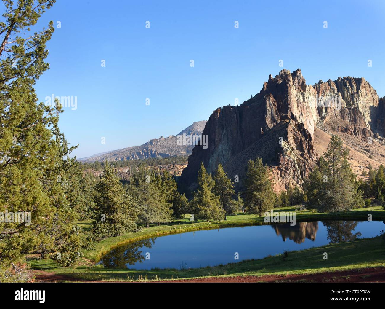 Blue sky and Cascade Mountain is reflected in small pond. Trees line ...