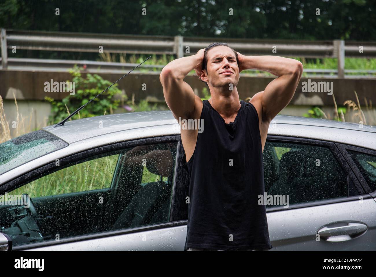 A man standing next to a car in the rain, sad because his vehicle broke ...