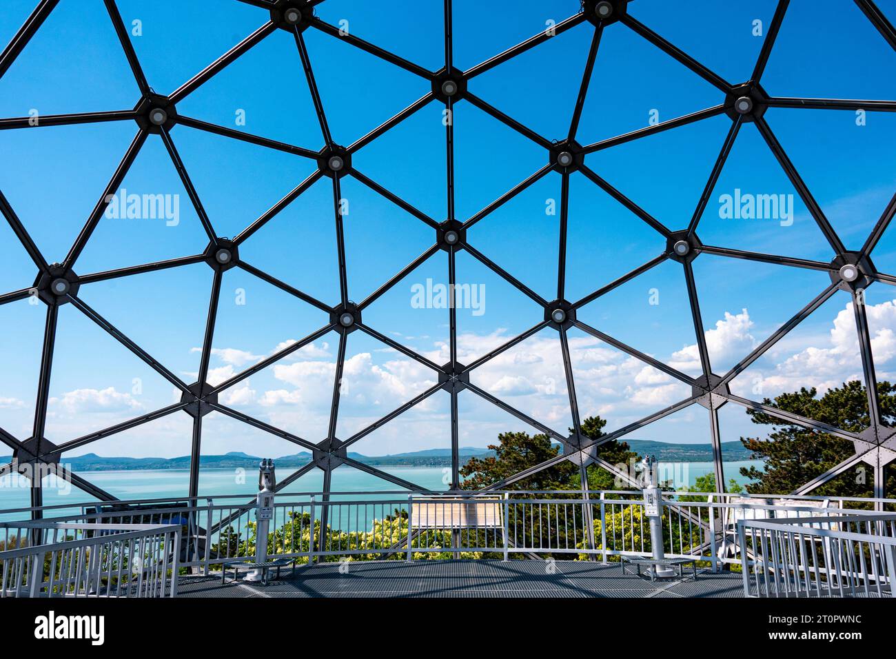 A lookout with a triangular metal grid structure on the shore of a lake ...