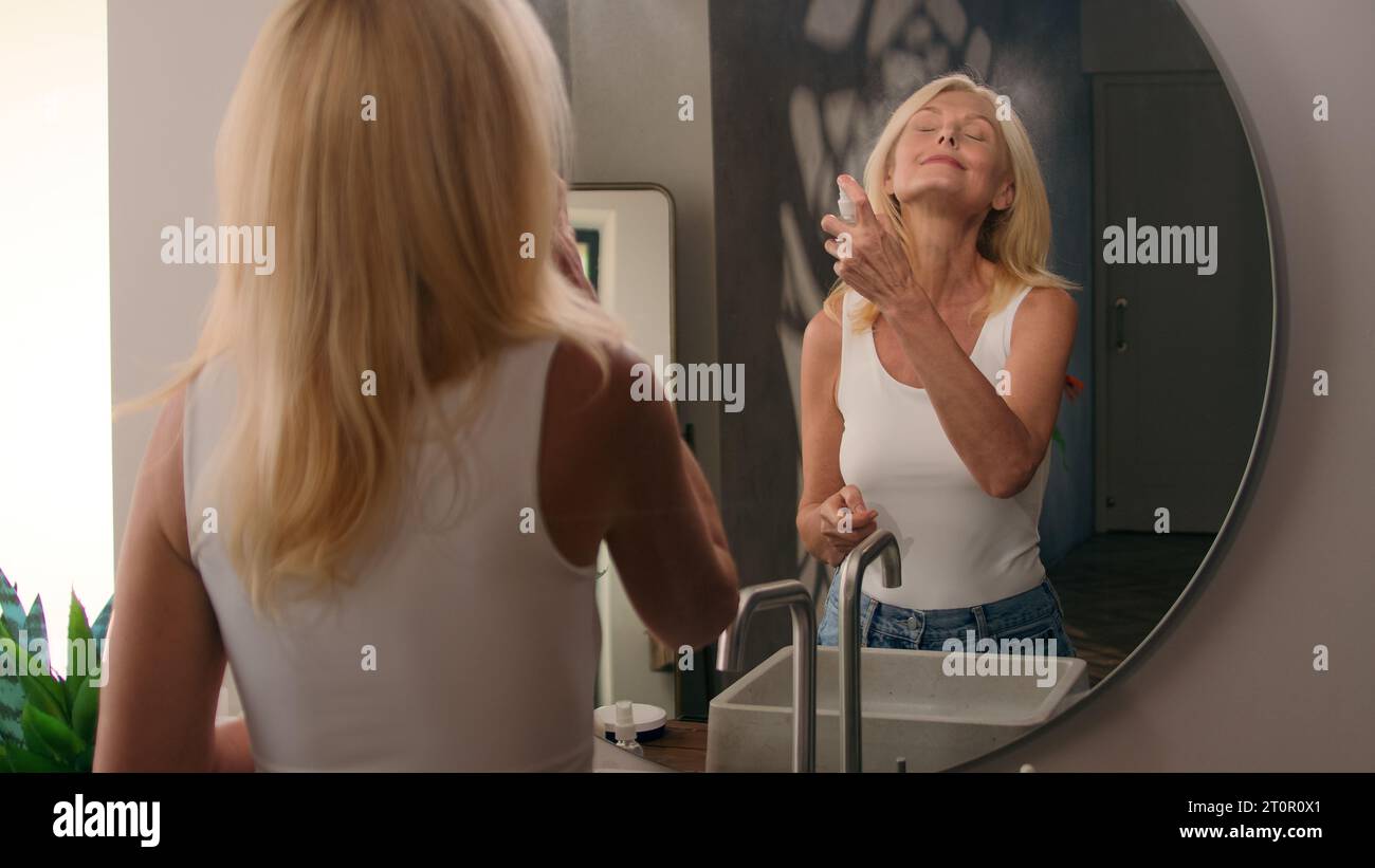 Smiling Caucasian senior mature woman look in bathroom mirror apply ...