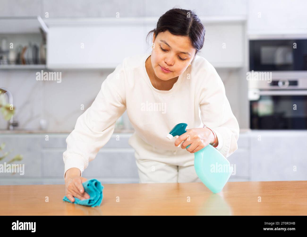 Smiling young woman wiping kitchen countertop with cleaning spray Stock ...