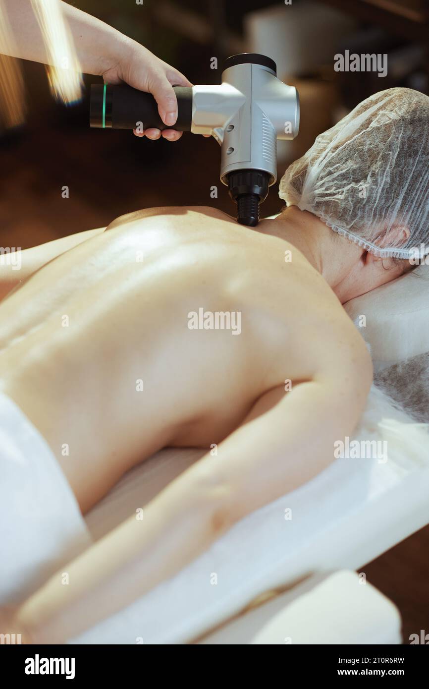 Healthcare time. massage therapist in spa salon with massage pistol massaging clients neck on ...