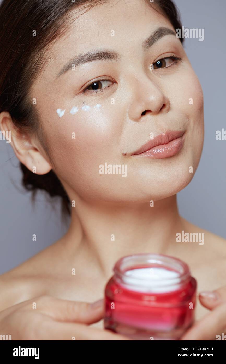 modern asian woman with facial cream jar and eye cream on face isolated ...