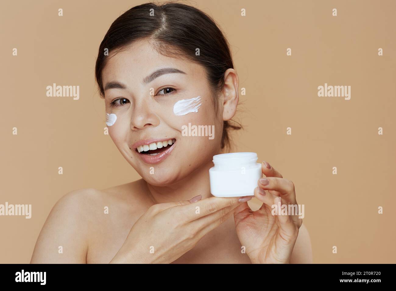 Portrait of young asian woman with facial cream jar and facial cream on ...