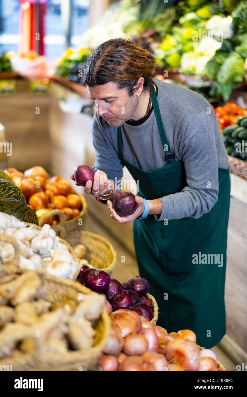 Male grocery store worker arranges red onion and other vegetables on ...