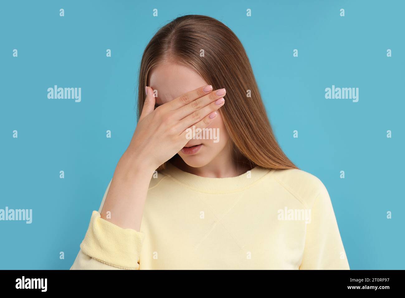 Embarrassed woman covering face with hand on light blue background ...