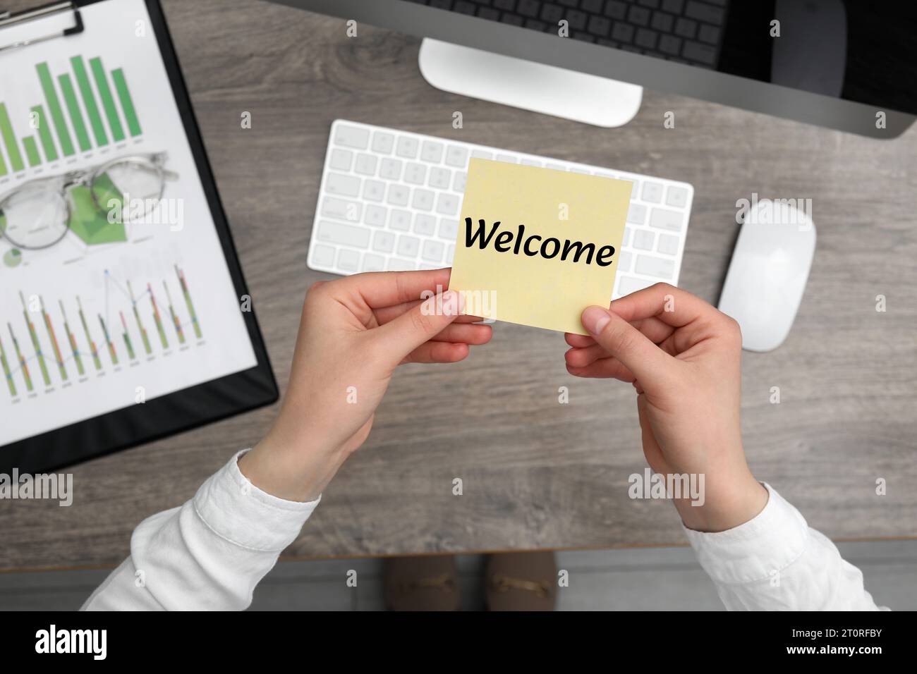 Woman holding paper note with word Welcome over her office desk, top ...