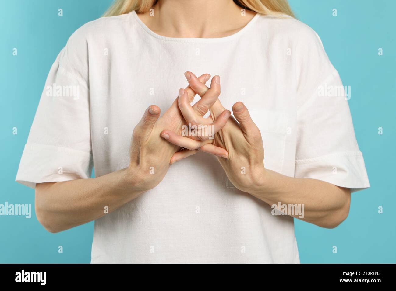 Woman cracking her knuckles on turquoise background, closeup. Bad habit ...