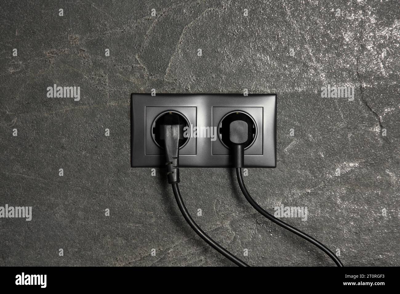 Power sockets with inserted plugs on dark grey wall. Electrical supply ...