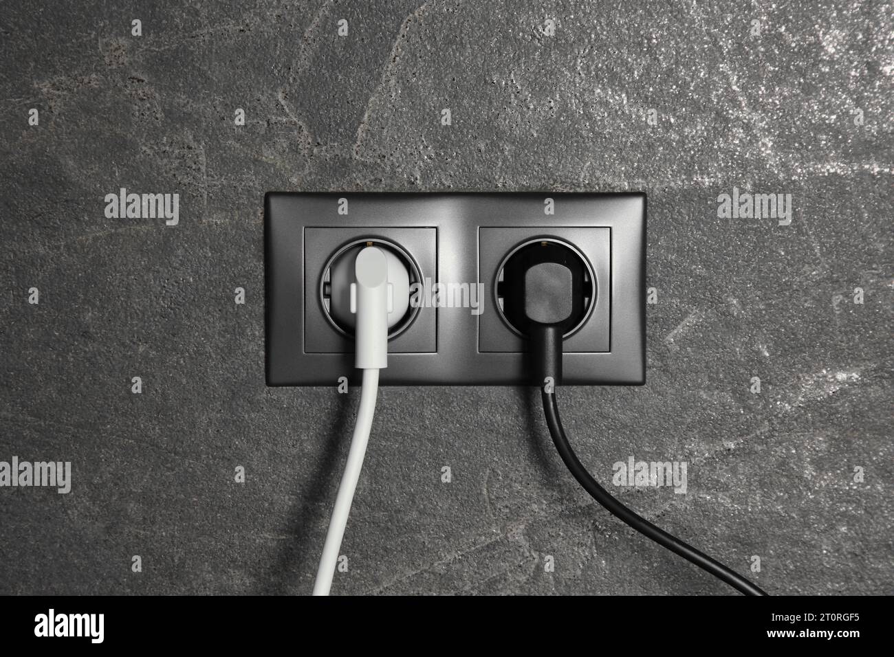 Power sockets with inserted plugs on dark grey wall. Electrical supply ...