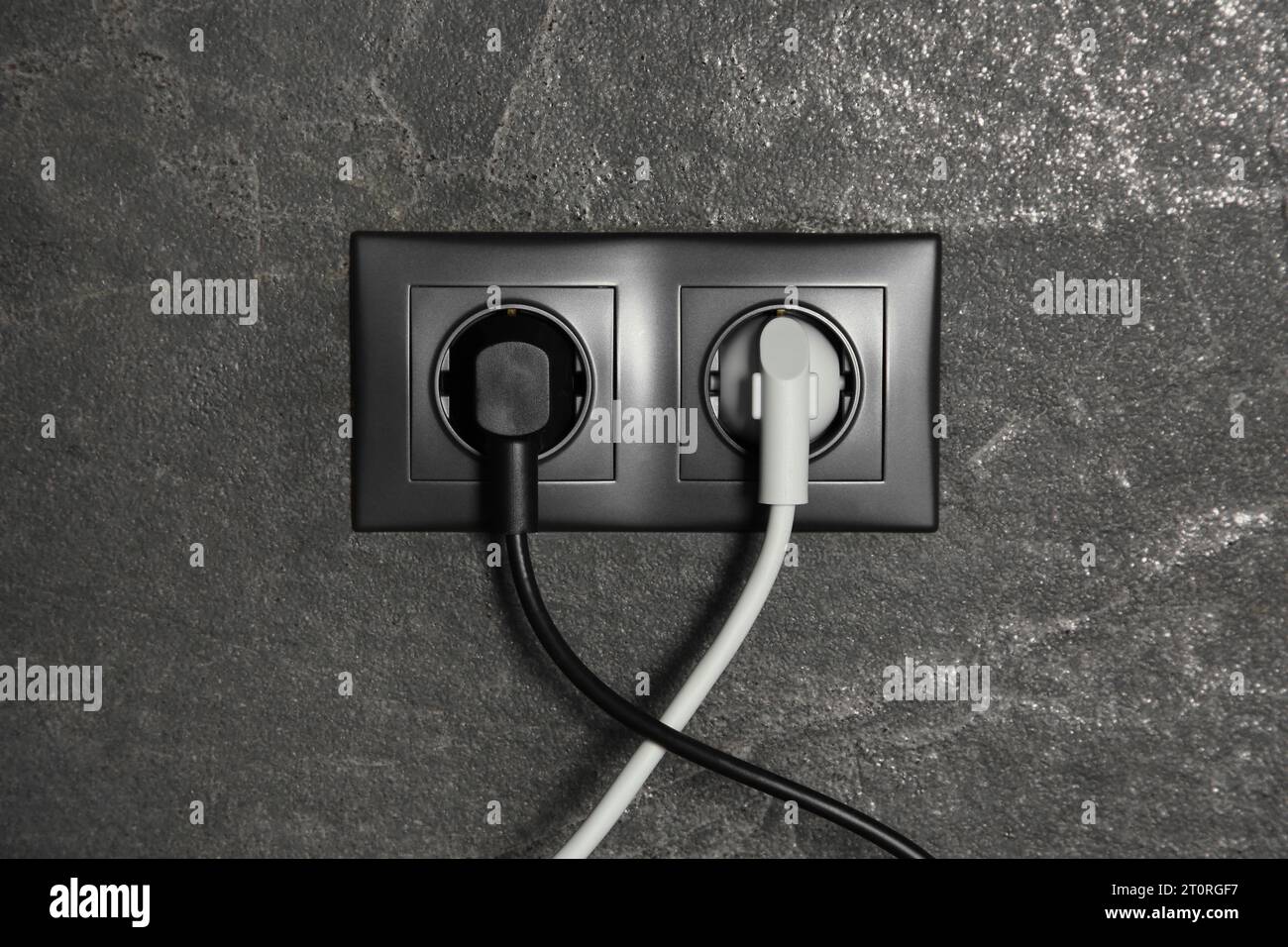 Power sockets with inserted plugs on dark grey wall. Electrical supply ...