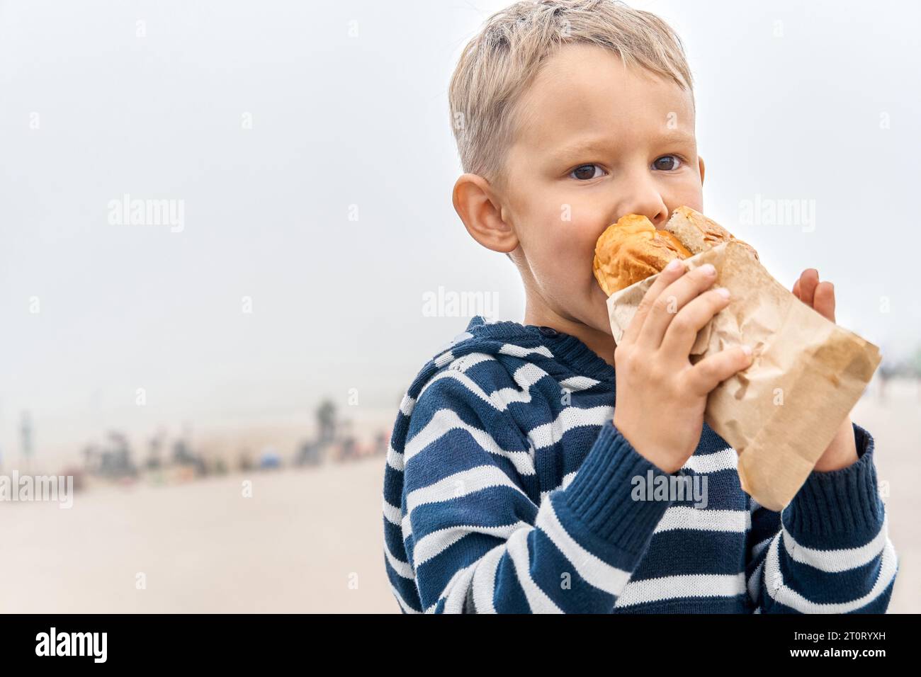 Hungry little boy with hood eats sandwich on misty day. Cute child ...