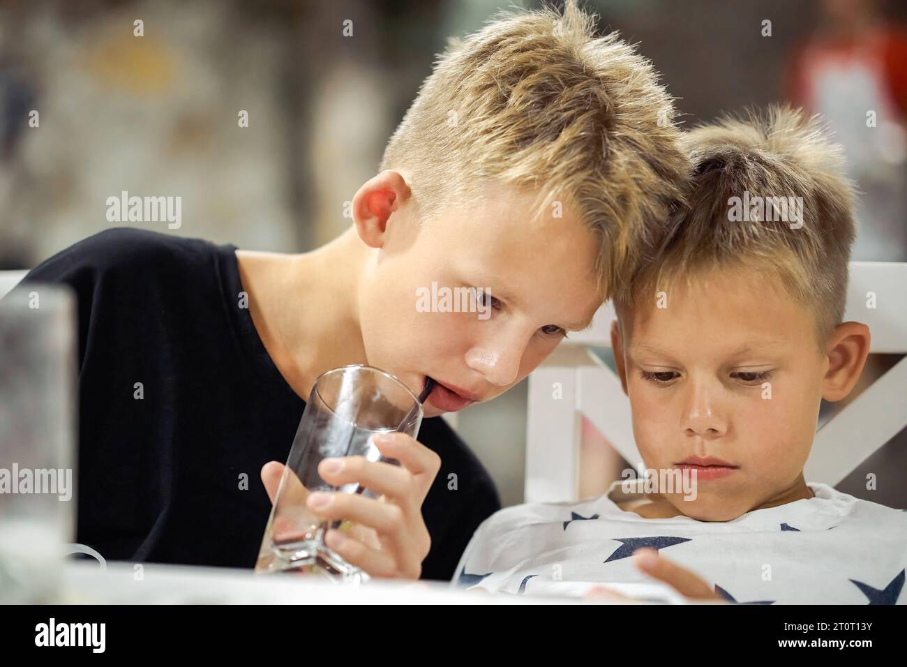 Concentrated boys watch video on mobile phone at restaurant table. Kid ...