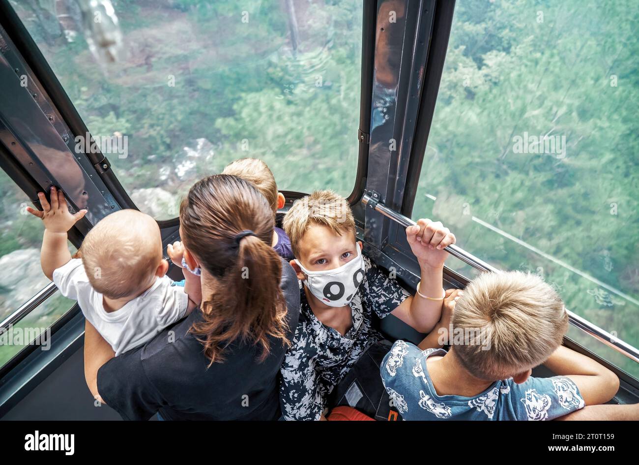 Mother with children ride funicular standing in cabin over green park ...