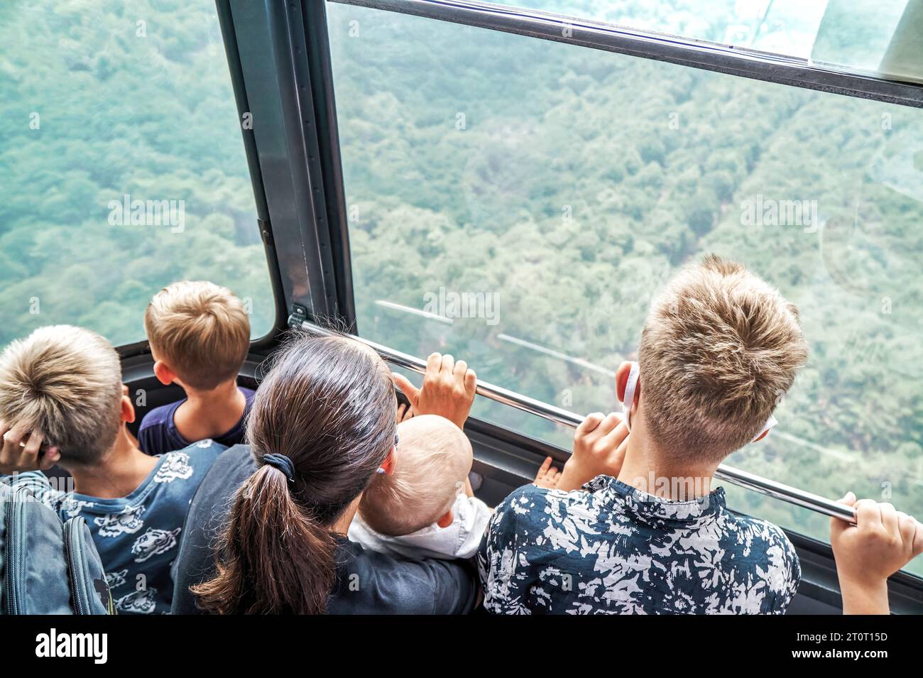 Mother with children ride funicular standing in cabin over green park ...