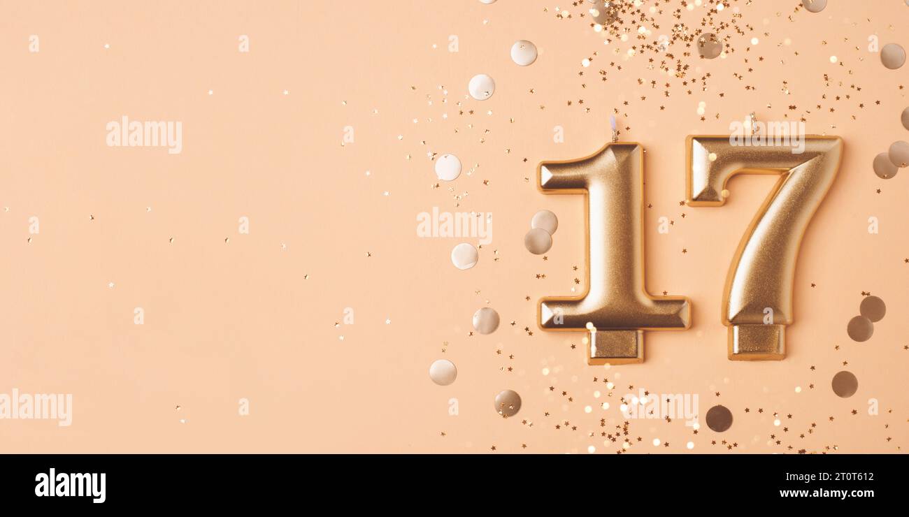 Gold candles in the form of number seventeen on peach background with ...