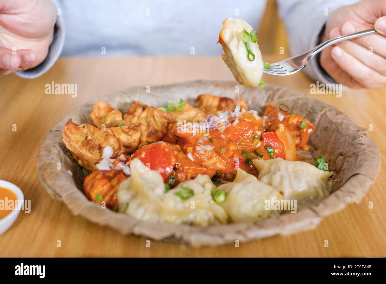 Man holding momo with fork over plate of assorted chicken dumplings ...