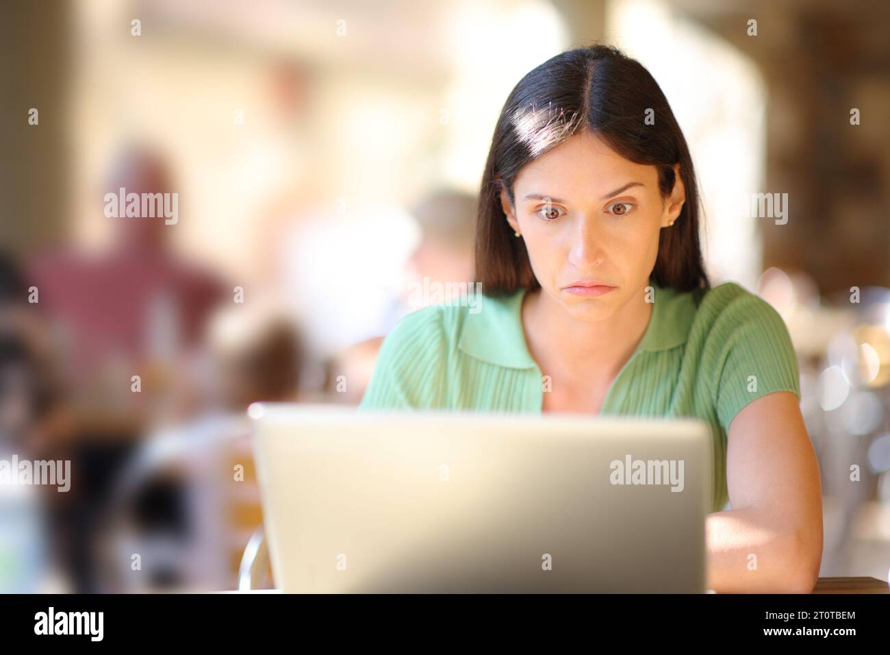 Front view portrait of a perplexed woman checking laptop in a ...