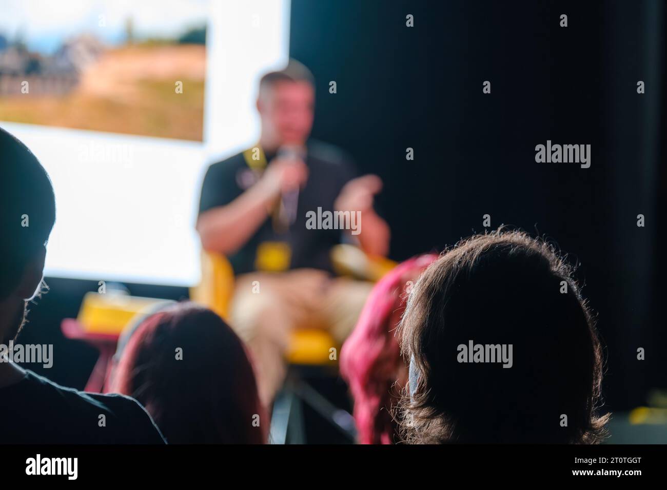 Male speaker standing on stage near big screen and giving presentation ...
